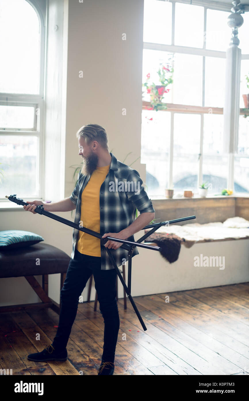Full length of photographer holding tripod while standing by window ...