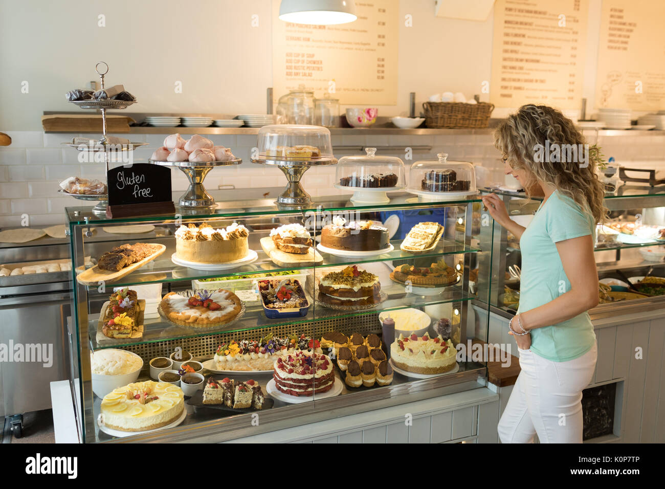 Side view of woman looking at cakes in display cabinet while standing ...