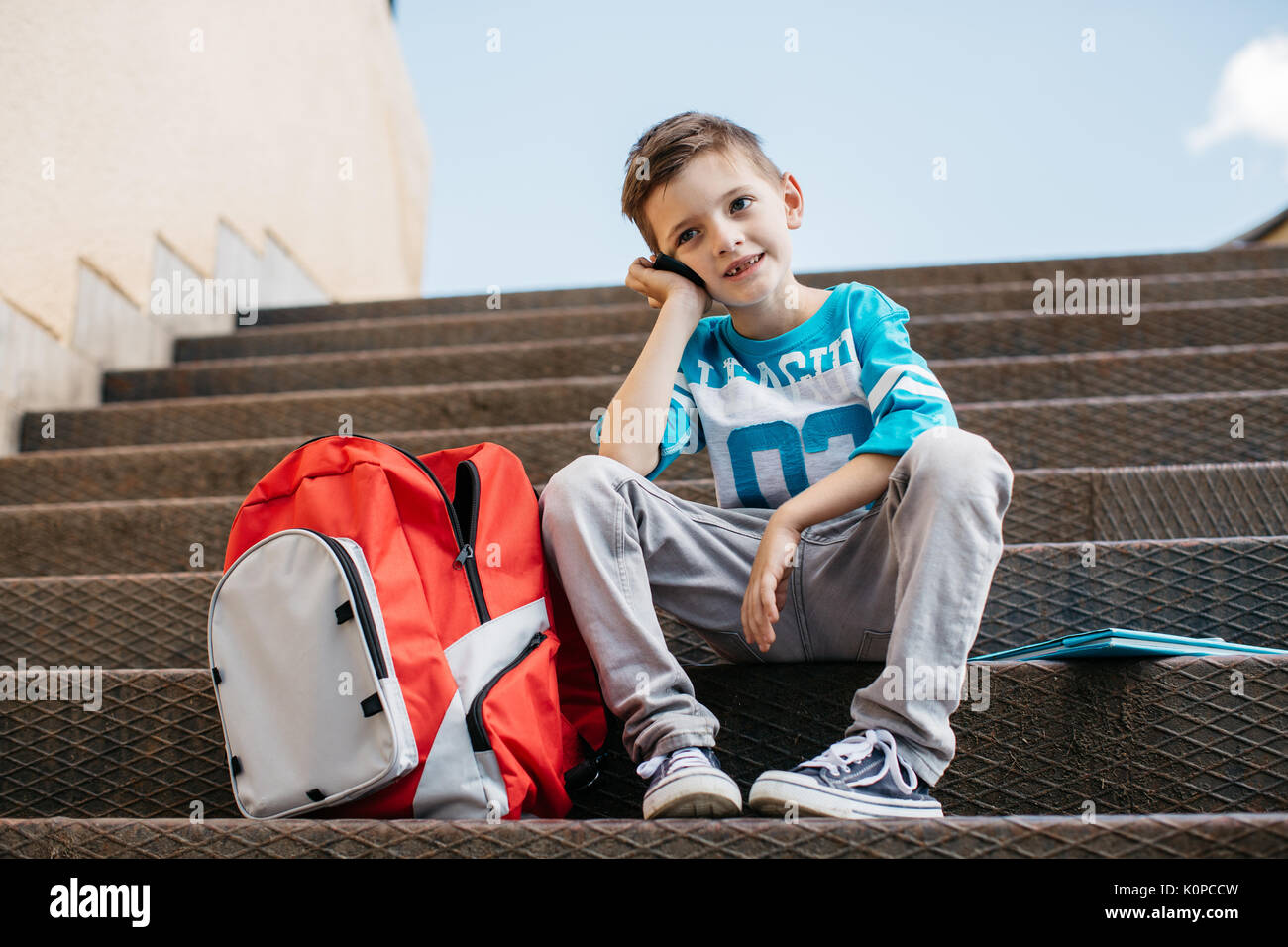 Front view of a cheerful student calling from his mobile outside school ...