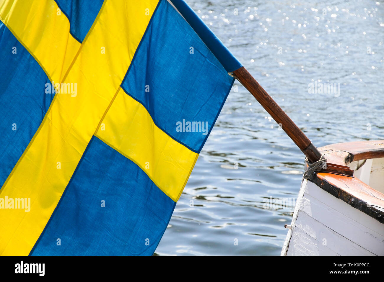 Swedish flag attached to wooden boat against water and sunny background ...