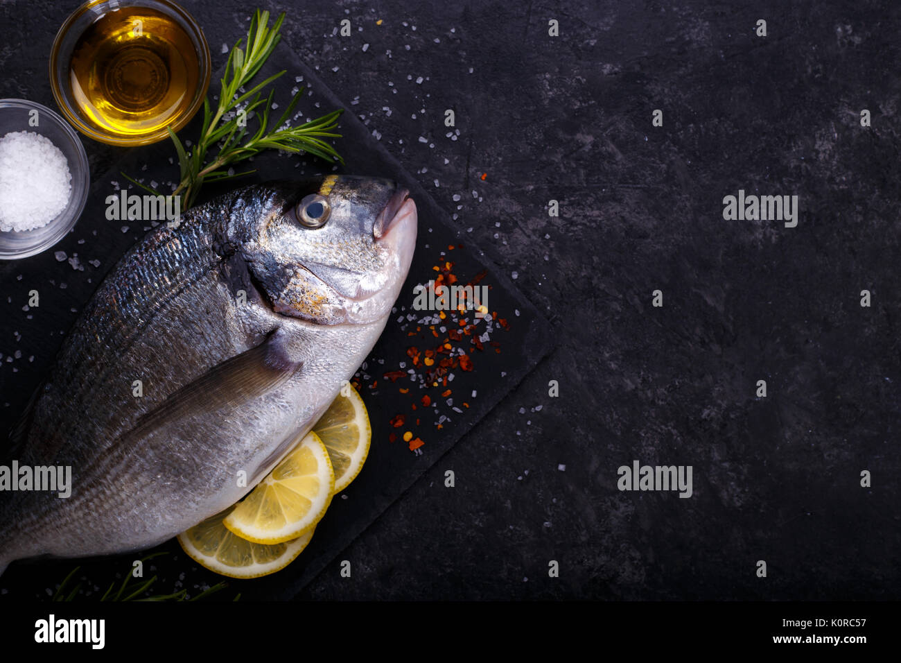 Fresh raw sea bream fish with lemon slices, salt, rosemary and olive ...