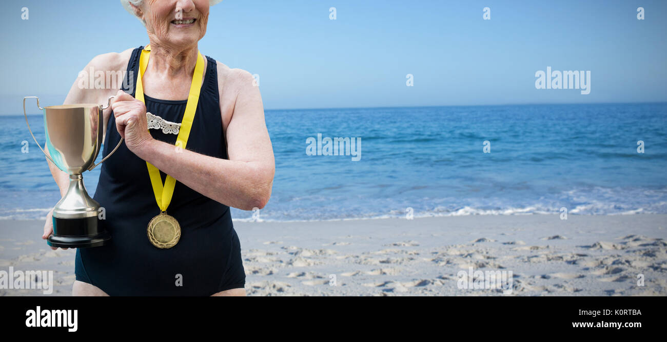 Portrait of confident swimmer showing trophy against beach against ...