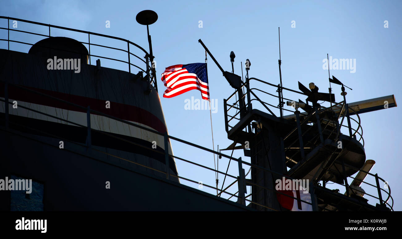 An American flag waves in the wind as the USS Cape Isabel arrives at ...