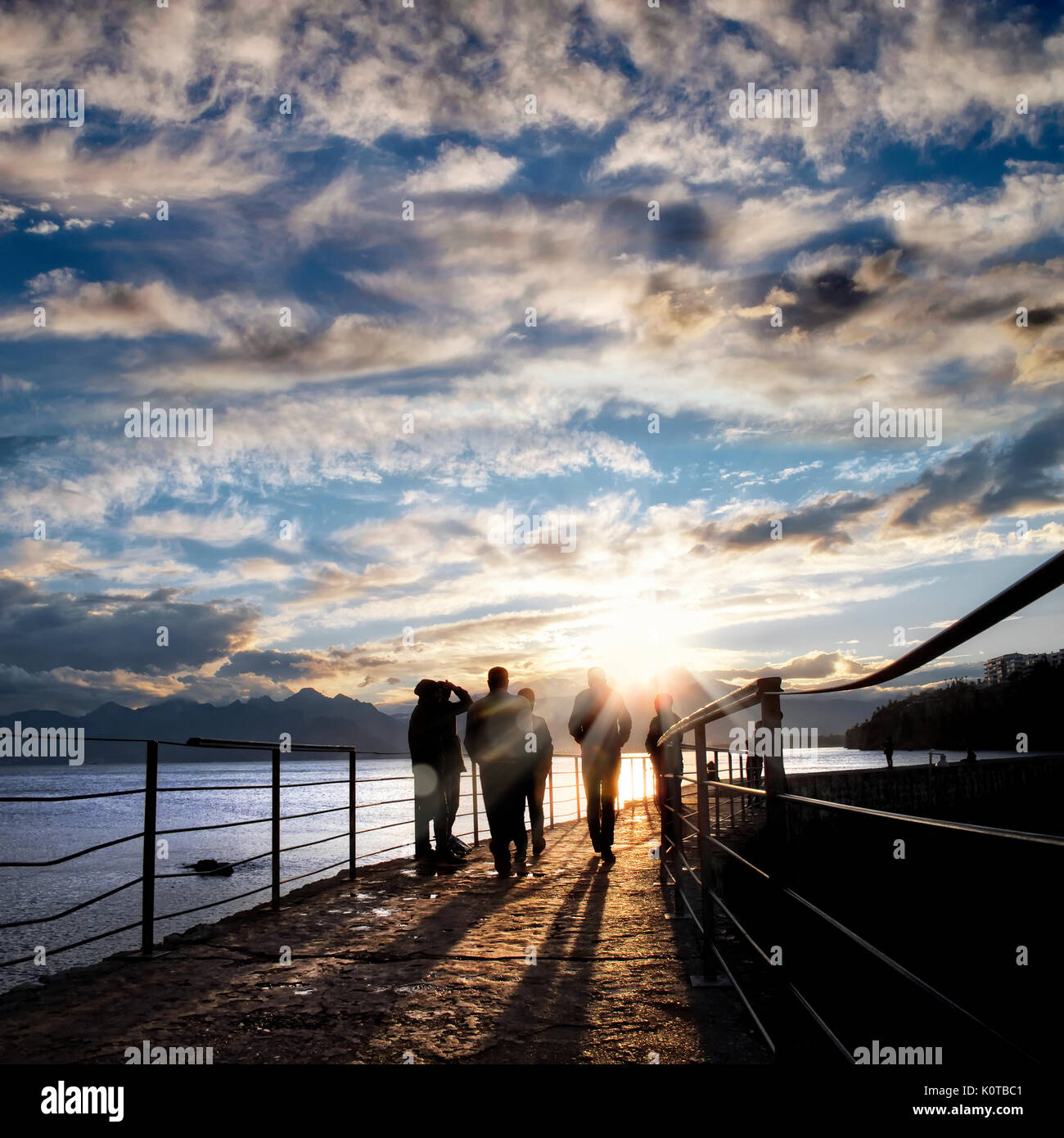 silhouetted people walking on street over sunset sky with sunbeam Stock ...