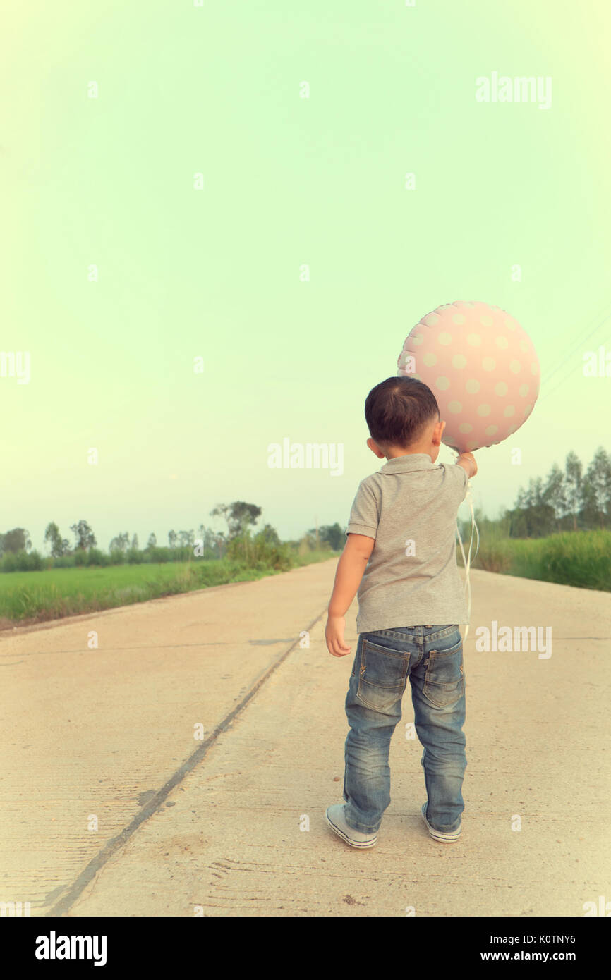 Little boy with a blue dot balloons looking at the in spring field ...