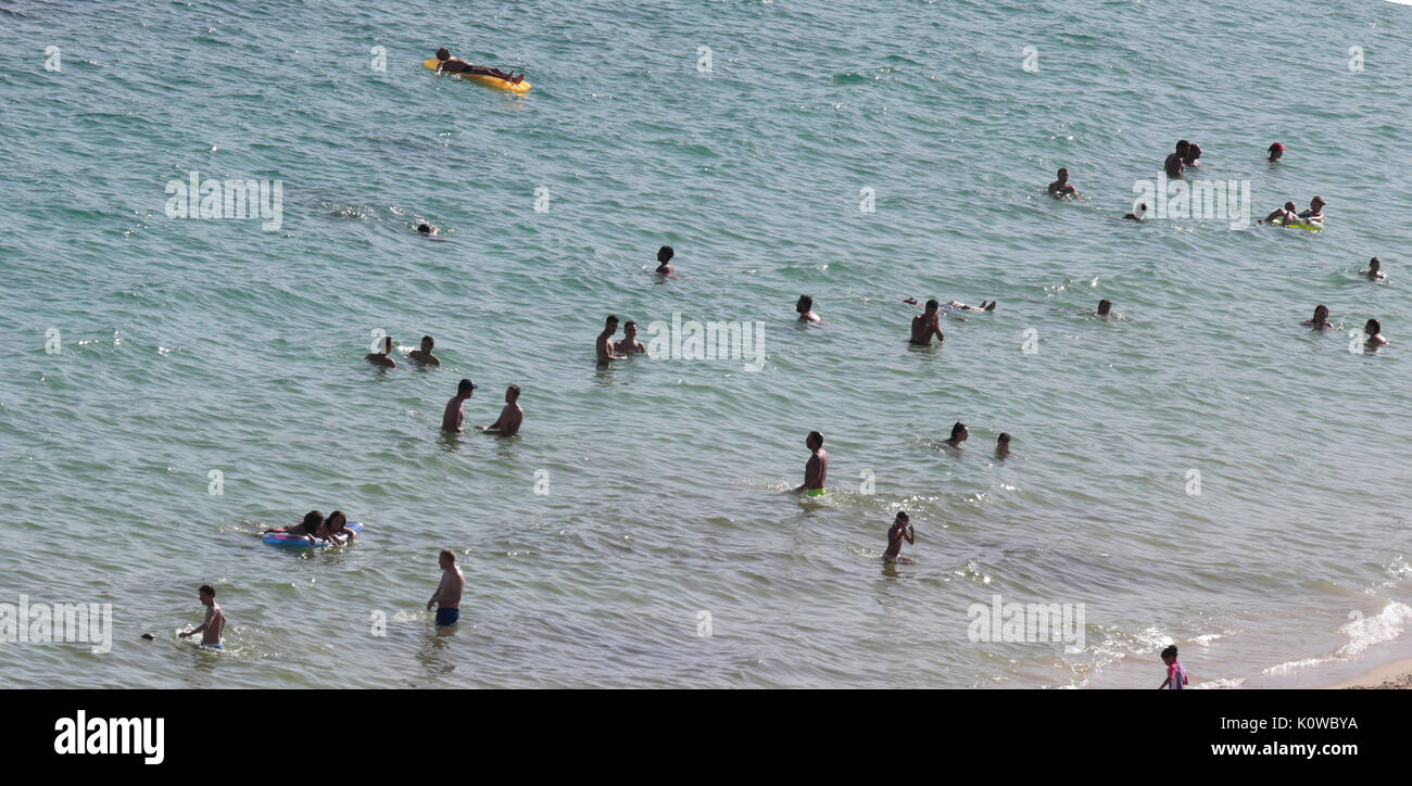 Tourists swim or enjoy marine activities as they sunbatthe in the beach ...