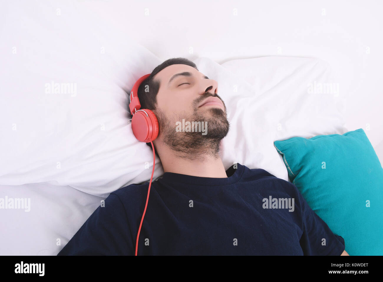 Attractive young man listening to music and relaxed in bed. Indoors ...