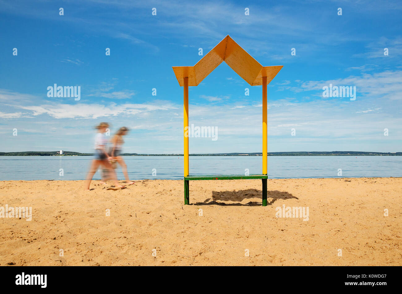 Empty beach with a metal yellow bench with a canopy on the coast ...