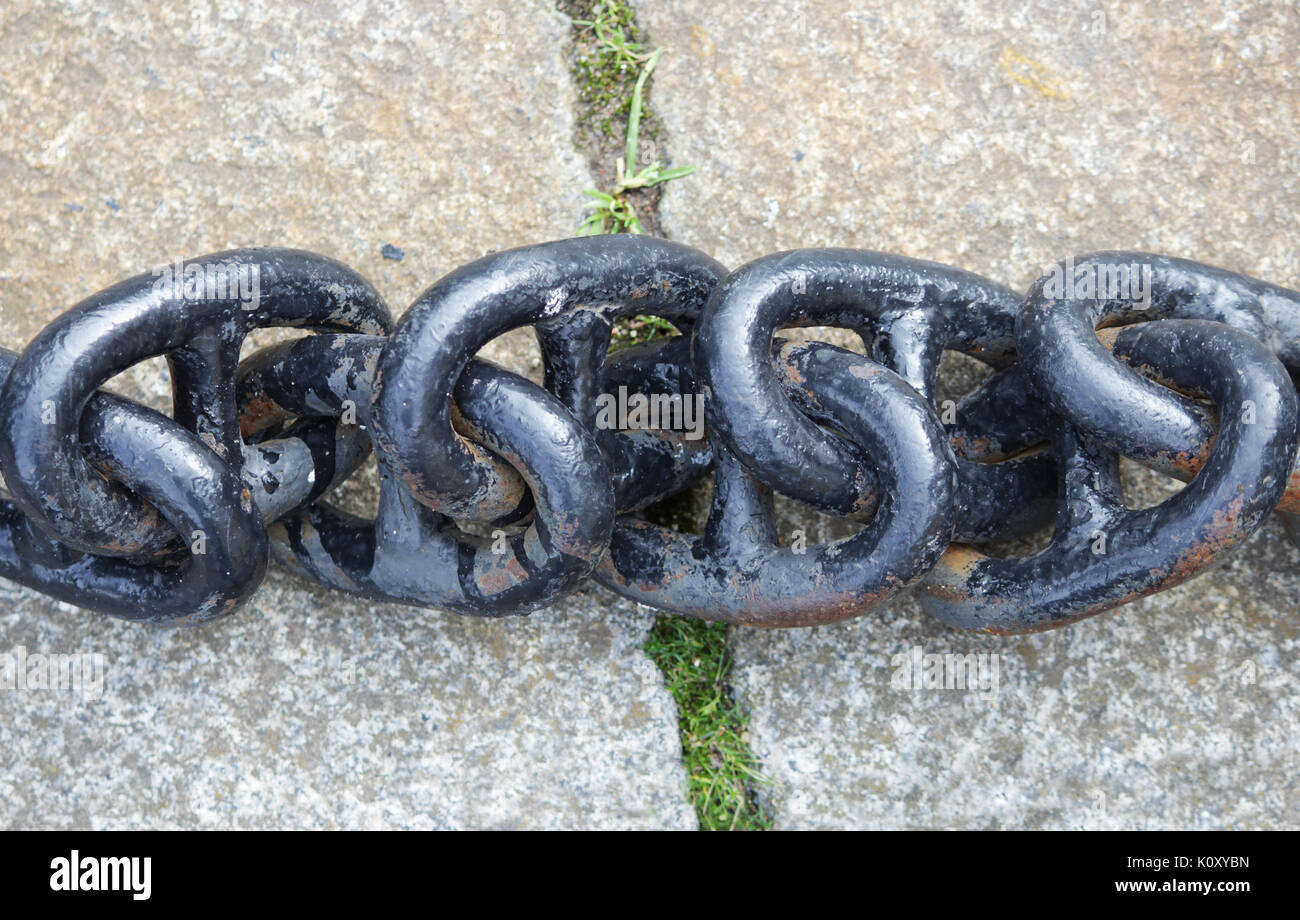 A black metal chain with large links lies on concrete slabs on the ...