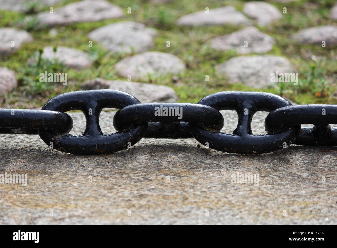 A black metal chain with large links lies on concrete slabs on the ...