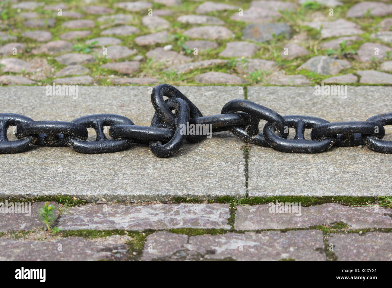 A black metal chain with large links lies on concrete slabs on the ...