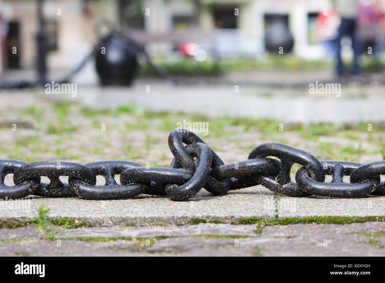 A black metal chain with large links lies on concrete slabs on the ...