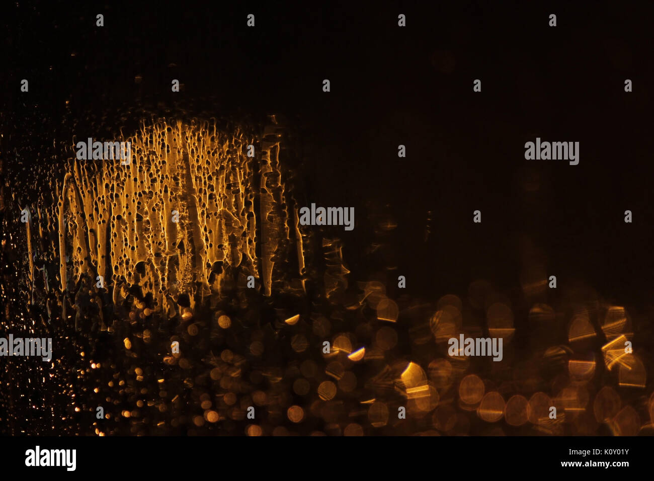 Drops of night rain on a glass of golden color, light of lanterns ...