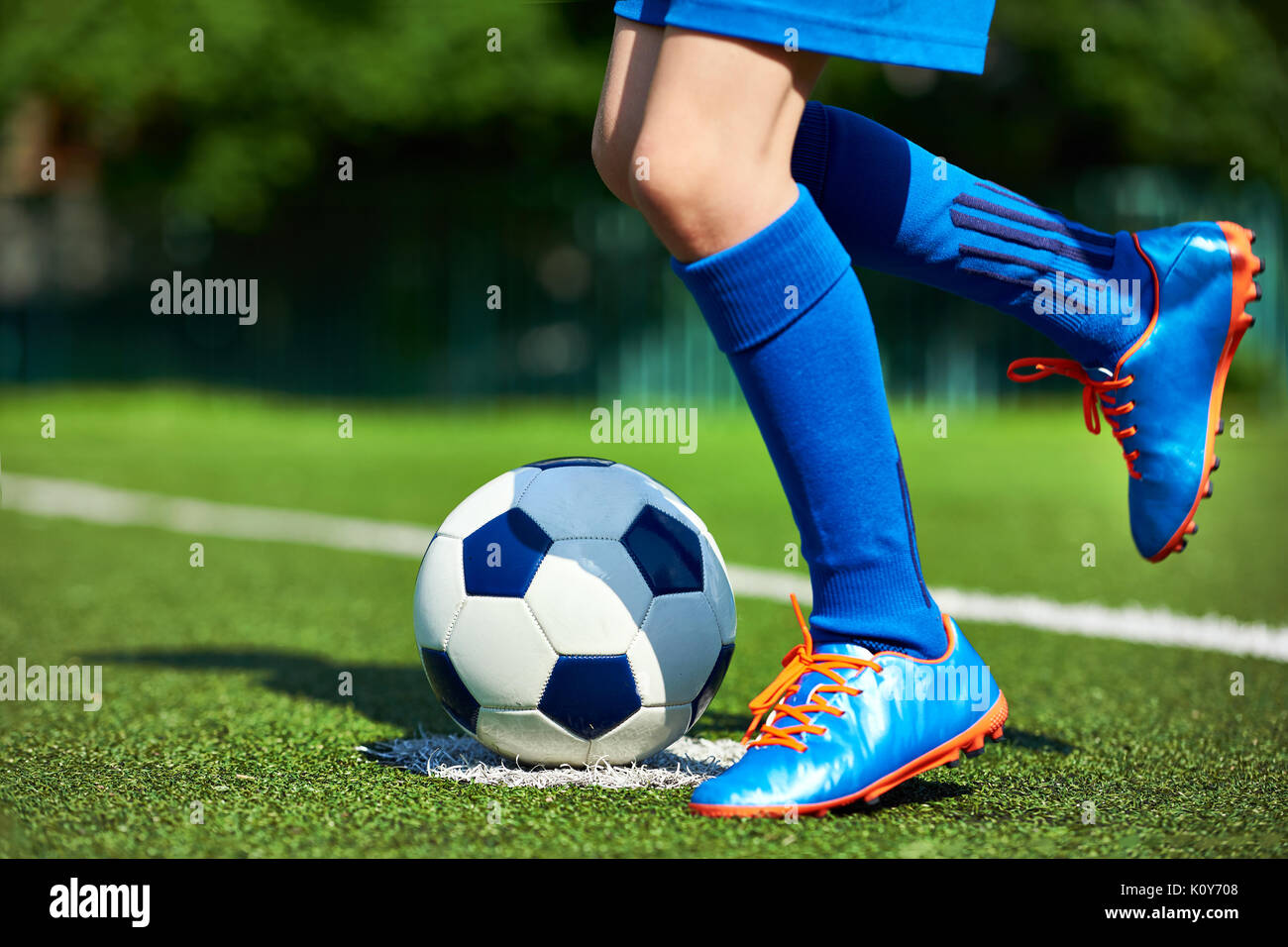 Legs of a football player boy in boots with a ball on the green lawn of ...