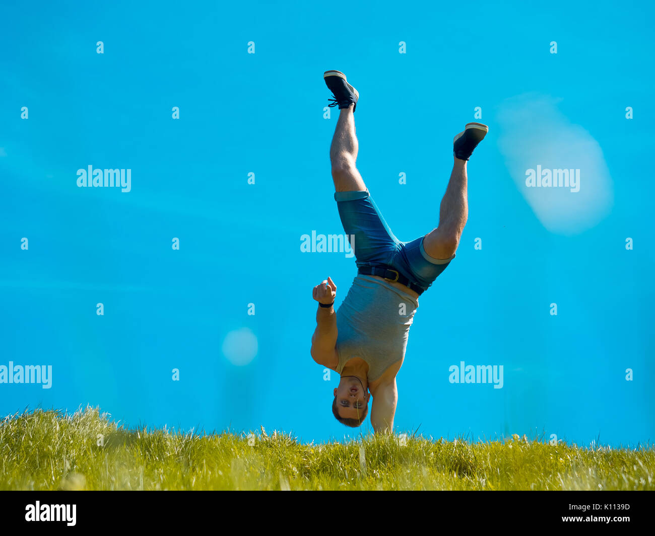 The guy is standing on one hand. Background blue sky. Below the green ...