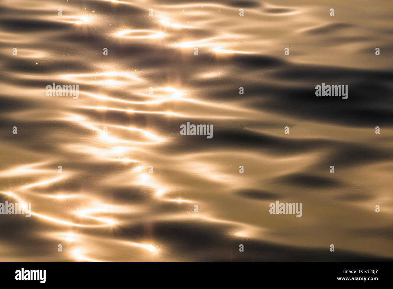 Water surface with moving wave of golden water reflecting sunlight ...