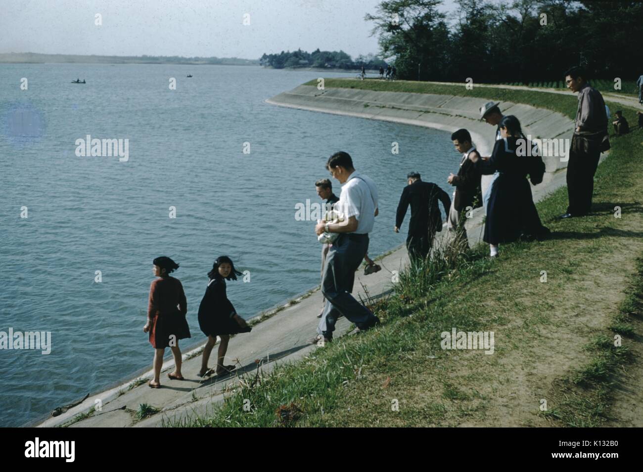 Japanese families walking down the embankment of a levee towards water ...