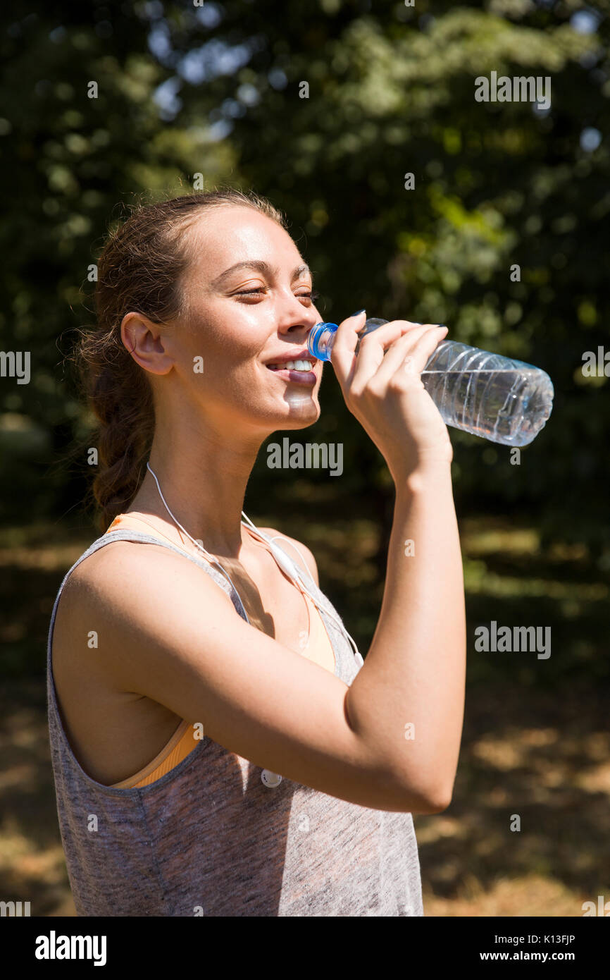 Pretty young woman drinking water during exercise in the park on a ...