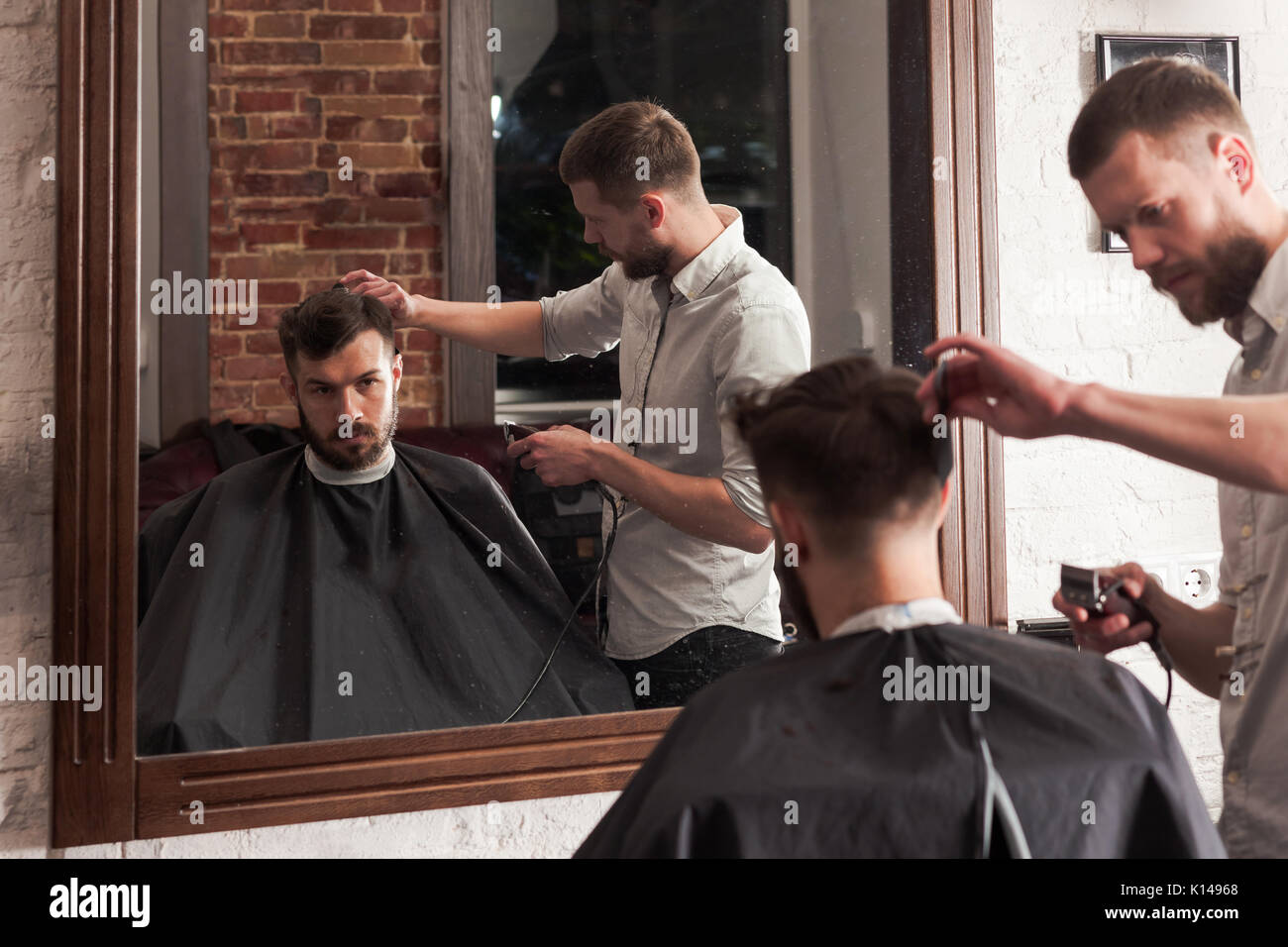 Young handsome barber making haircut of attractive man in barbershop ...