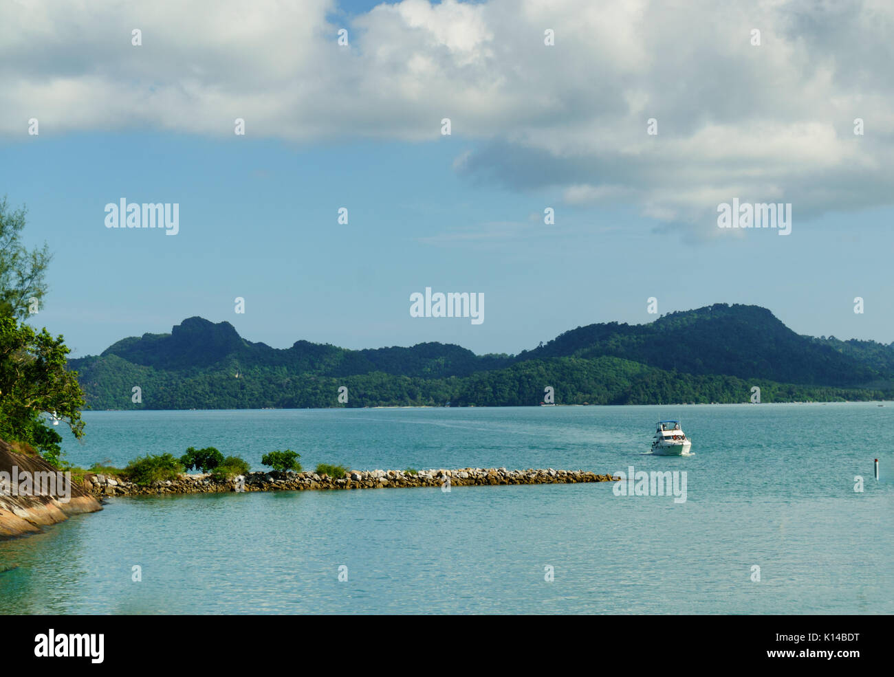 Boat approaching rocky outcrop with blue water and hills in the Stock ...