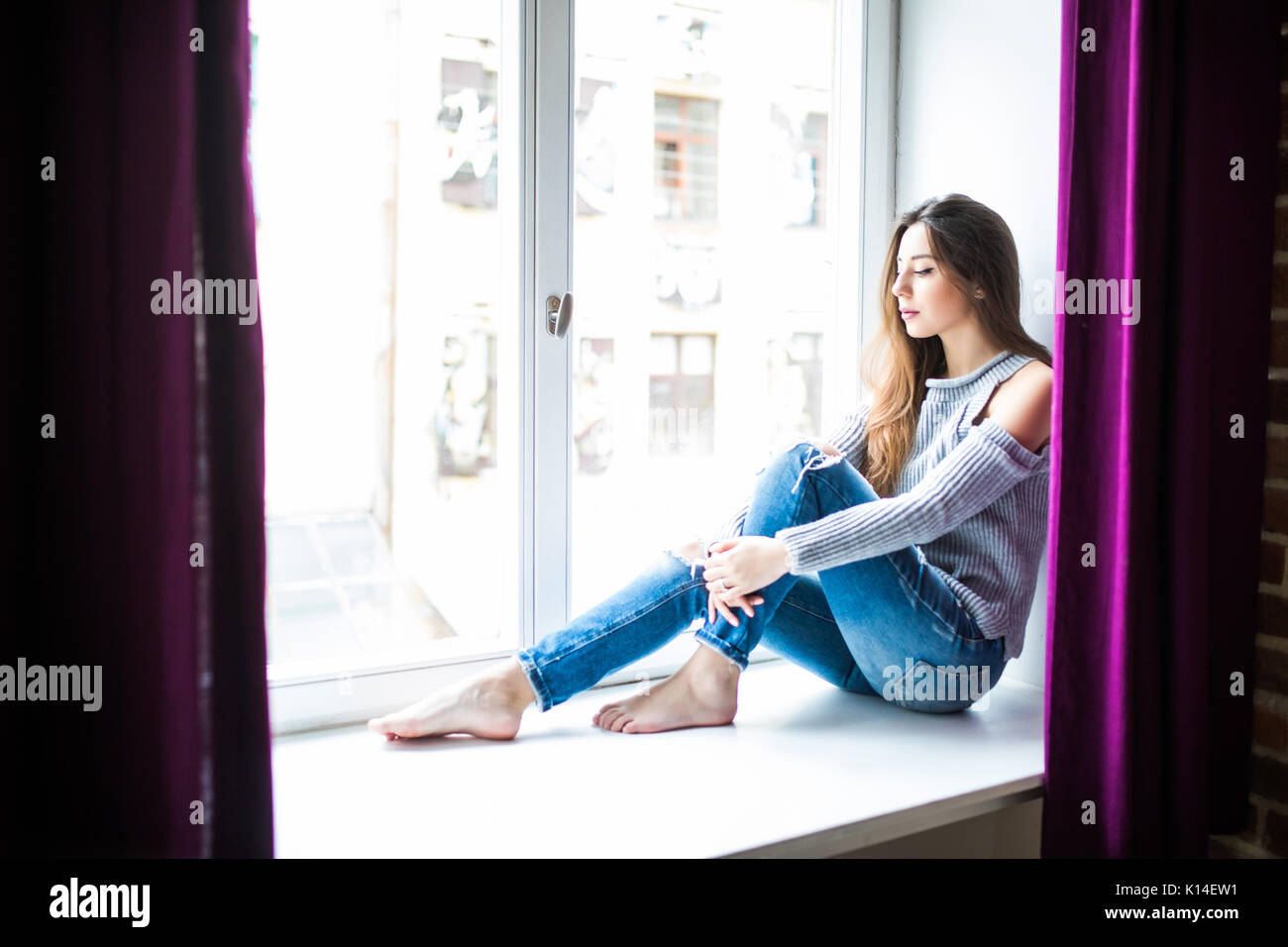 Beautiful woman sitting on window sill at home Stock Photo - Alamy