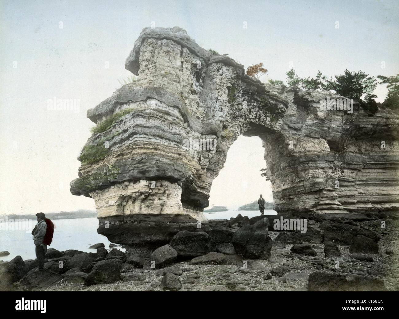 A natural stone archway towers over a figure while another person looks ...
