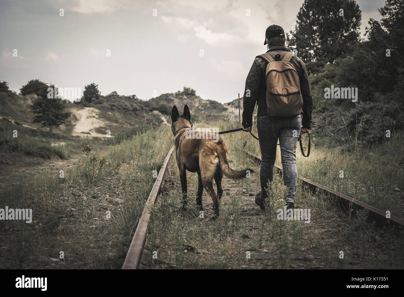 A woman with a backpack and her dog crossing the path of old rails in ...
