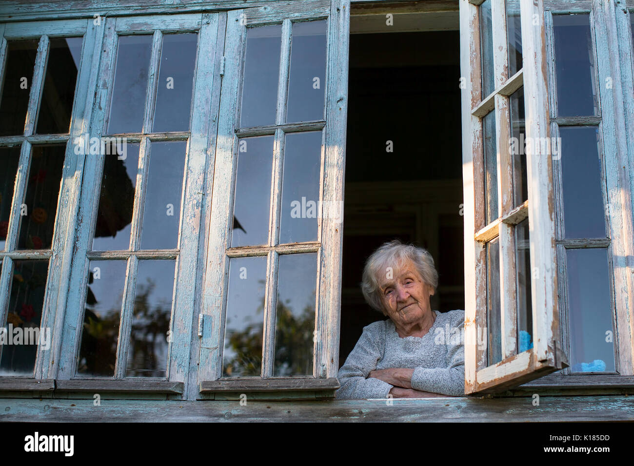 Grandmother, an elderly woman looks from the window of the farmhouse ...