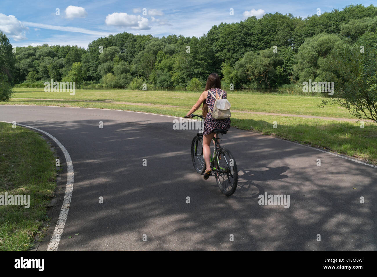 Girl riding a bicycle. Back view. Forest and clouds in the background ...
