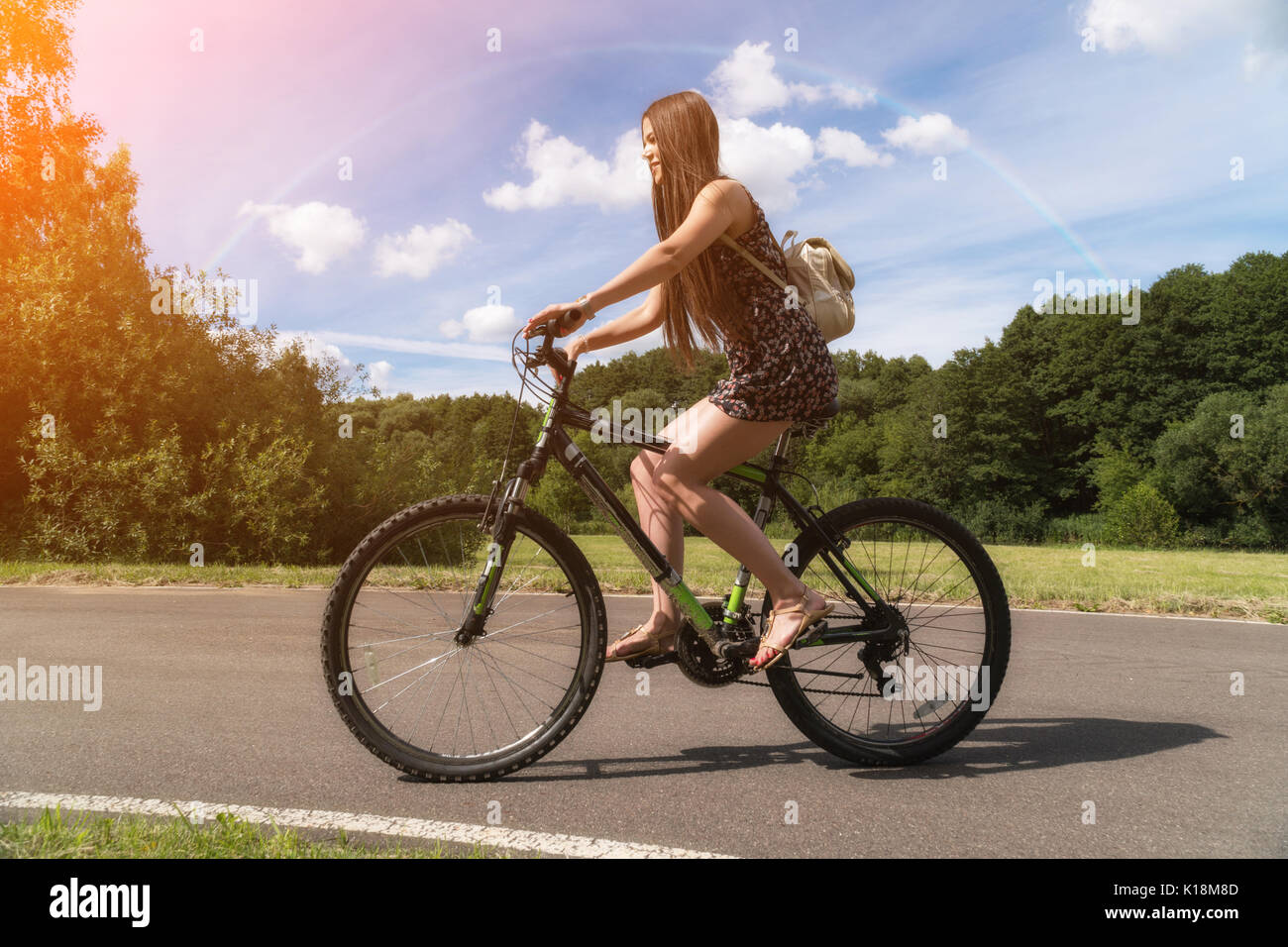 Girl riding a bicycle. Side view. Forest and clouds in the background ...