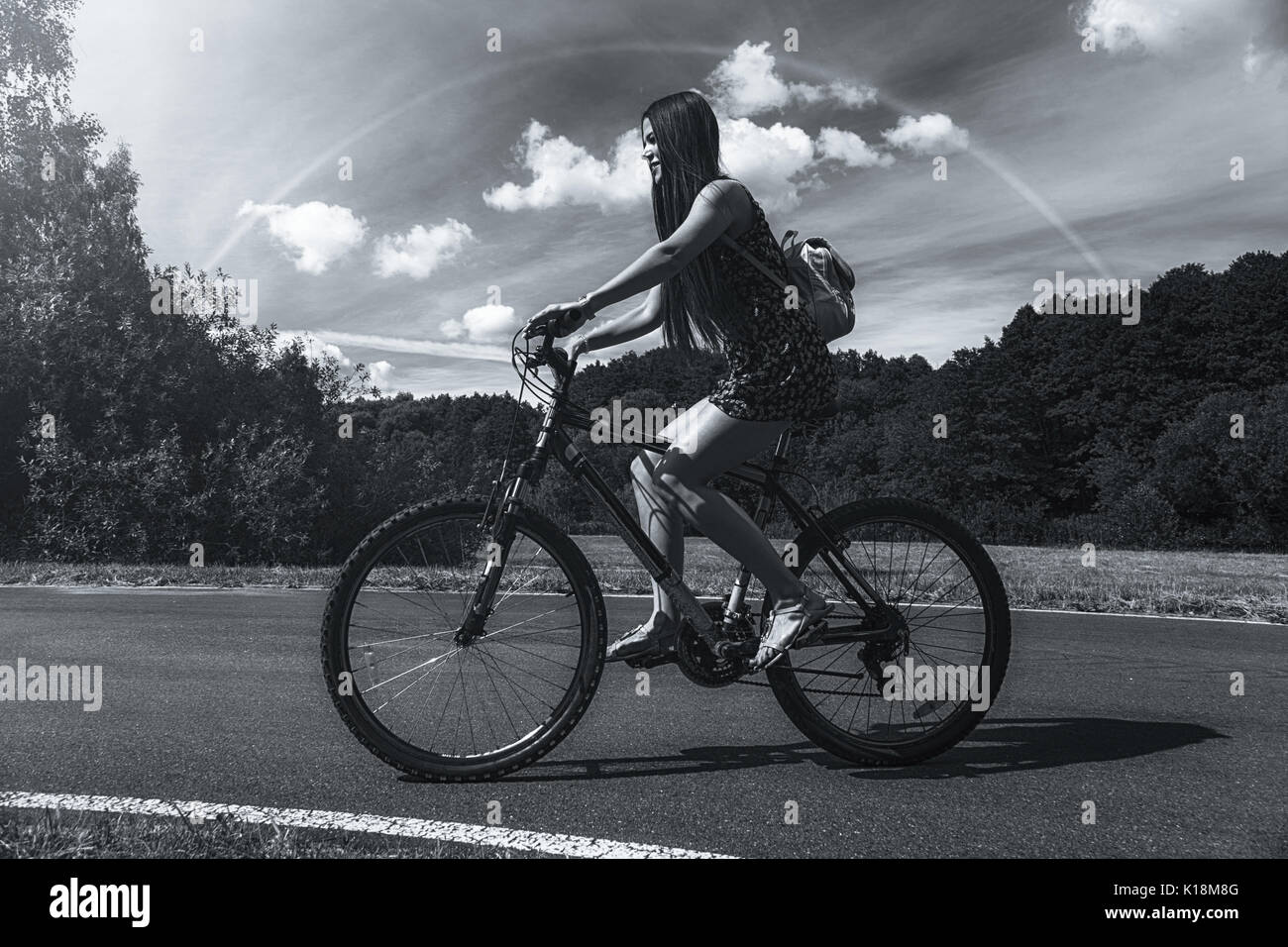 Girl riding a bicycle. Side view. Forest and clouds in the background ...