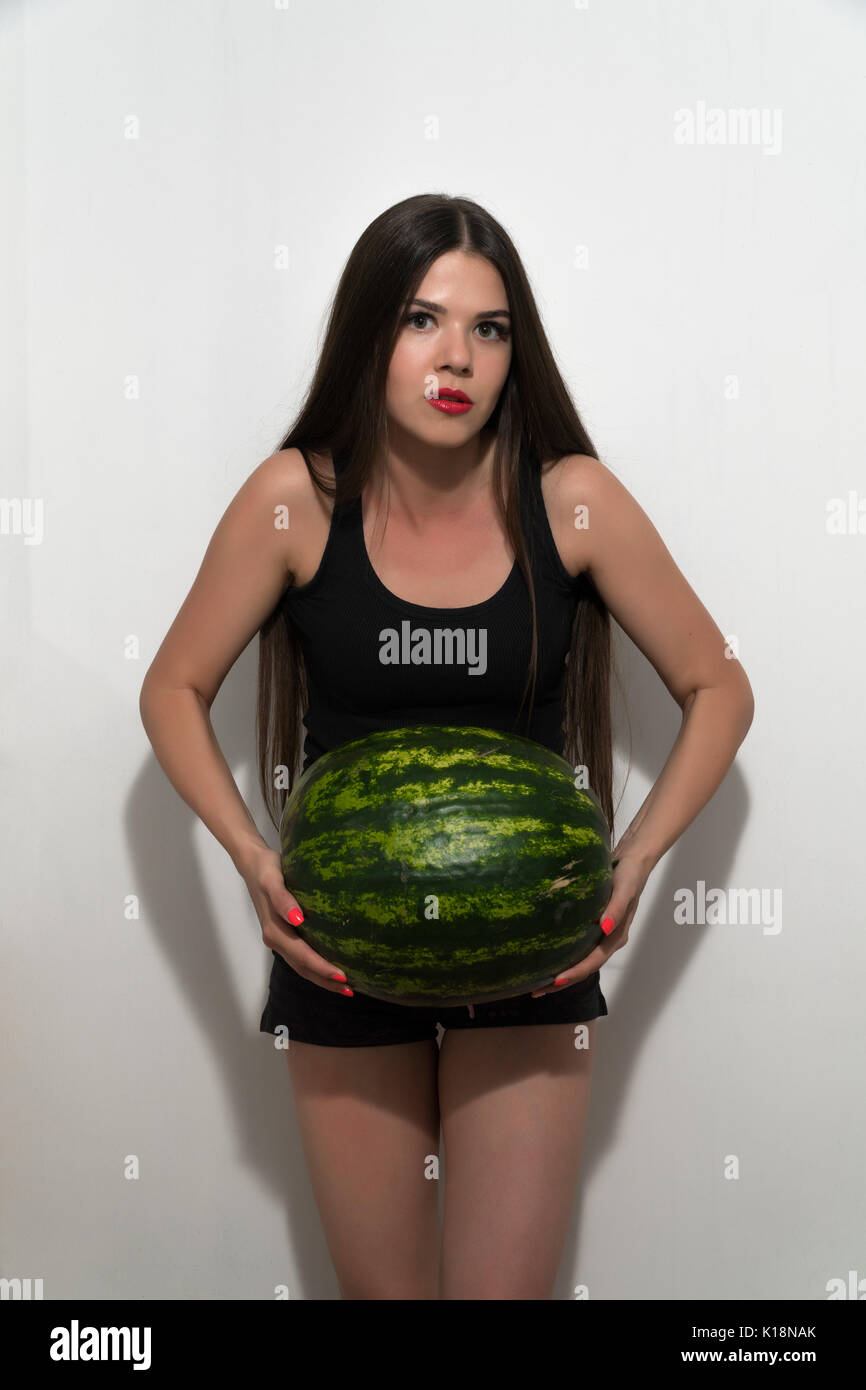 The girl is holding a big watermelon in her hands. The brunette is ...