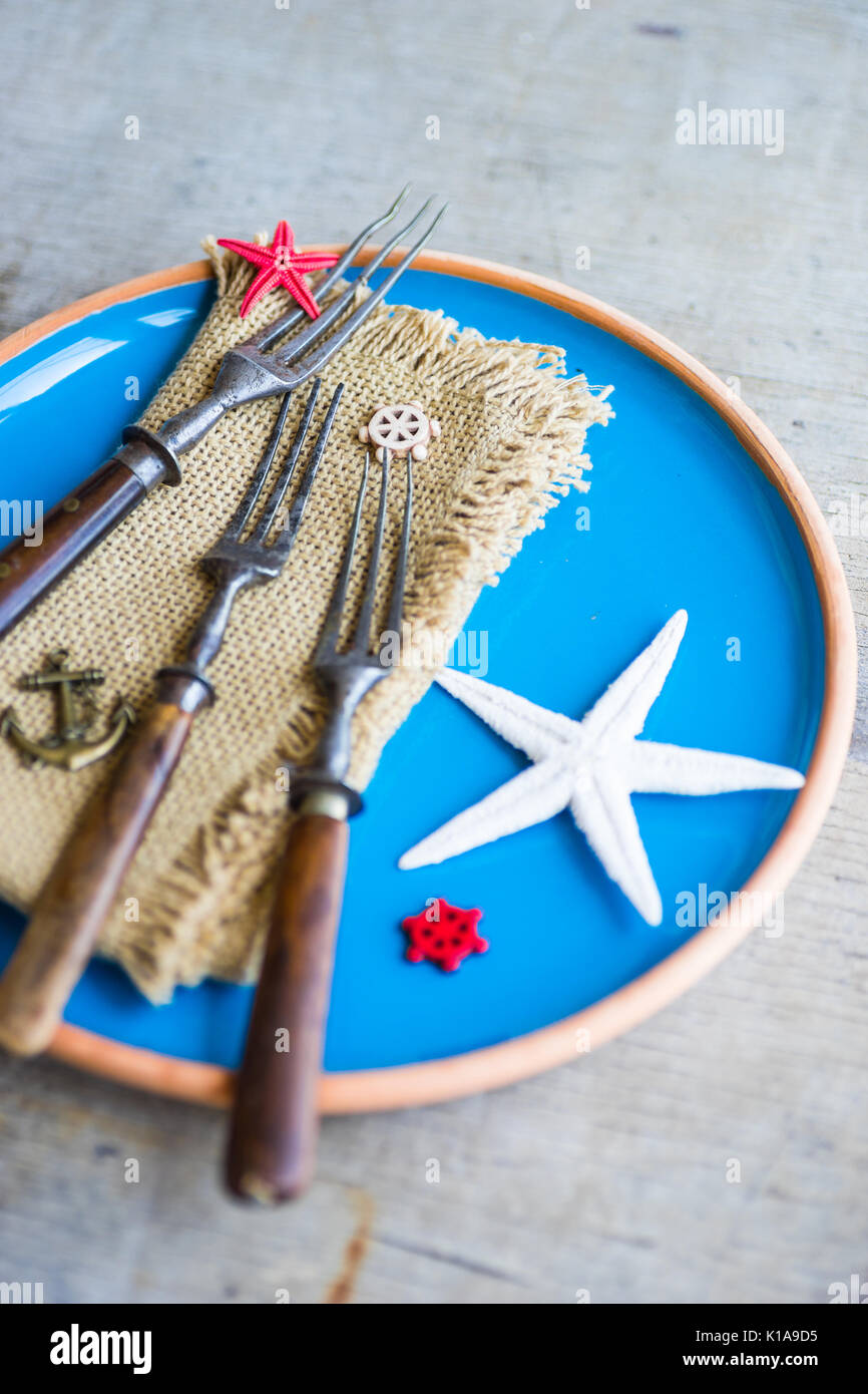 Summer vacation marine table setting with rustic plates and silverware ...