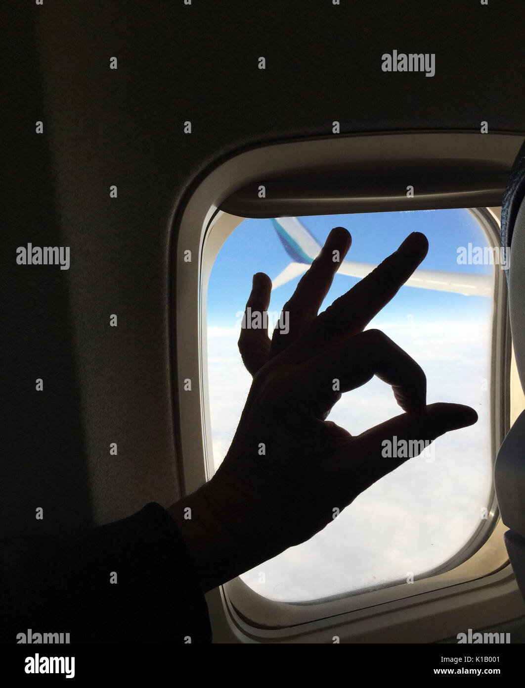 A passenger makes an OK sign with his hand against the plane window at ...