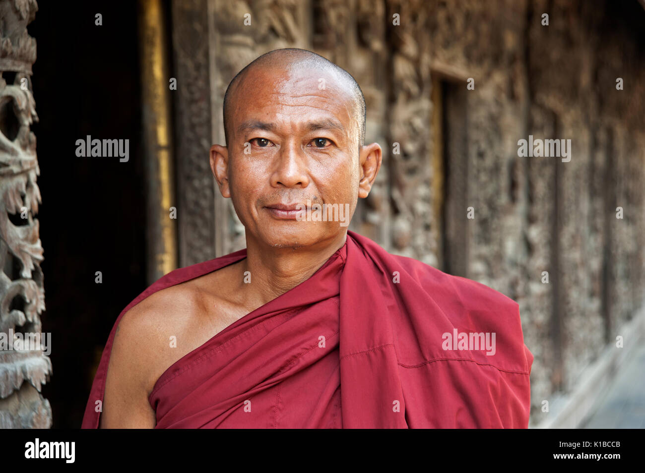 Portrait of a Buddhist monk standing in front of the carved teak panels ...