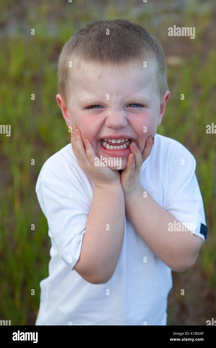 A young boy grinning with his hands around his face Stock Photo - Alamy