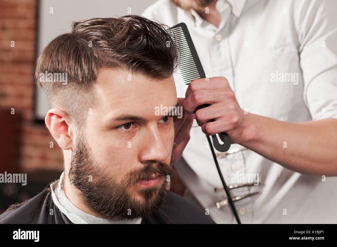 The hands of barber making haircut to young man in barbershop Stock ...