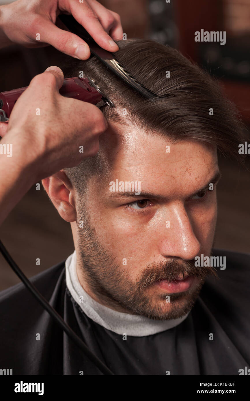 The hands of barber making haircut to young man in barbershop Stock ...