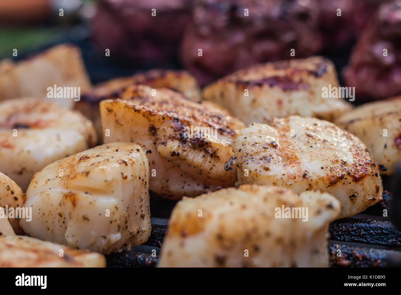 Mini beef sliders and fresh sea scallops being cooked on a charcoal ...
