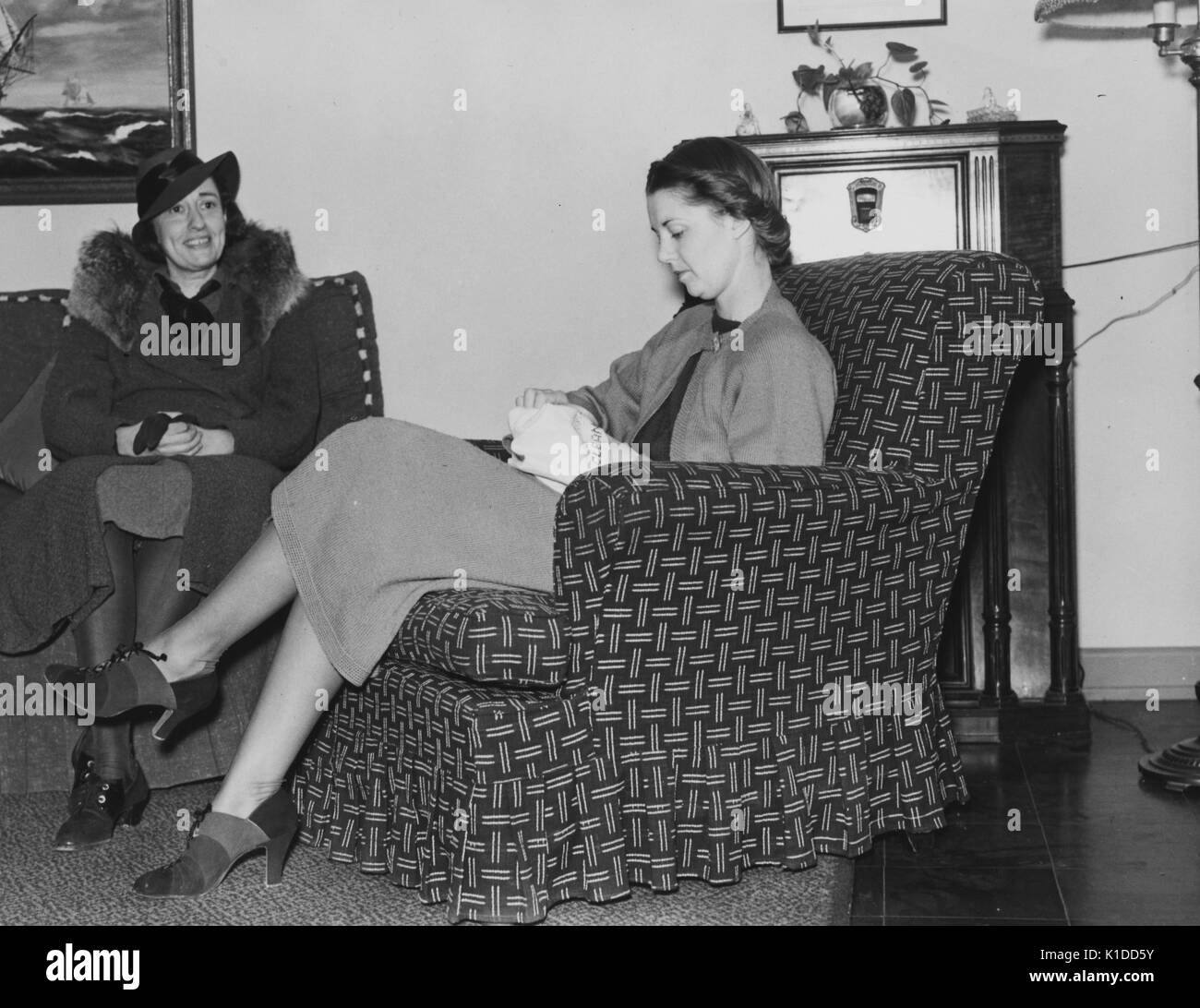 Two female neighbors sitting in chairs in a suburban living room during ...