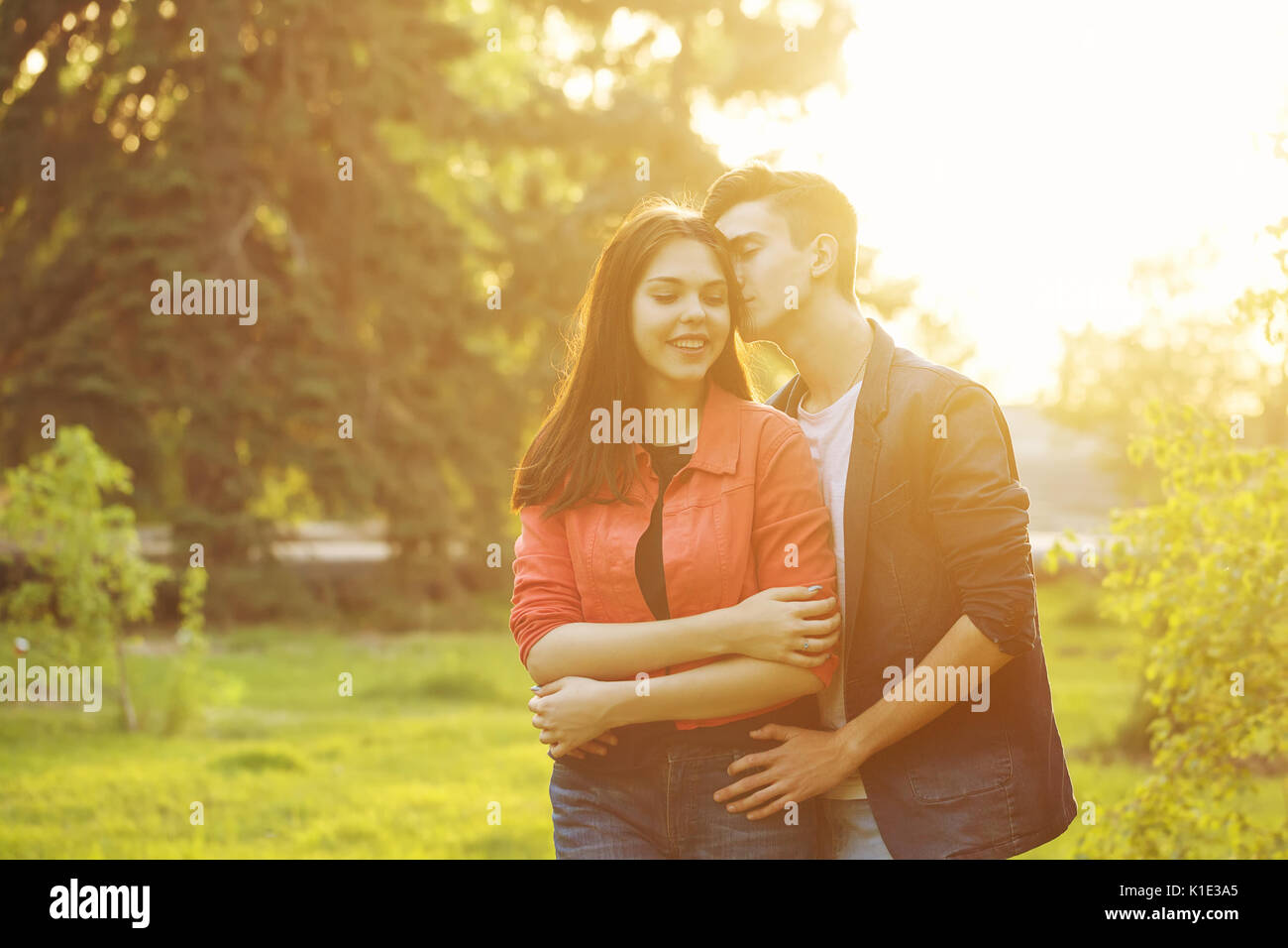 Date of teenagers. The guy hugs her friend from behind. He whispers in ...