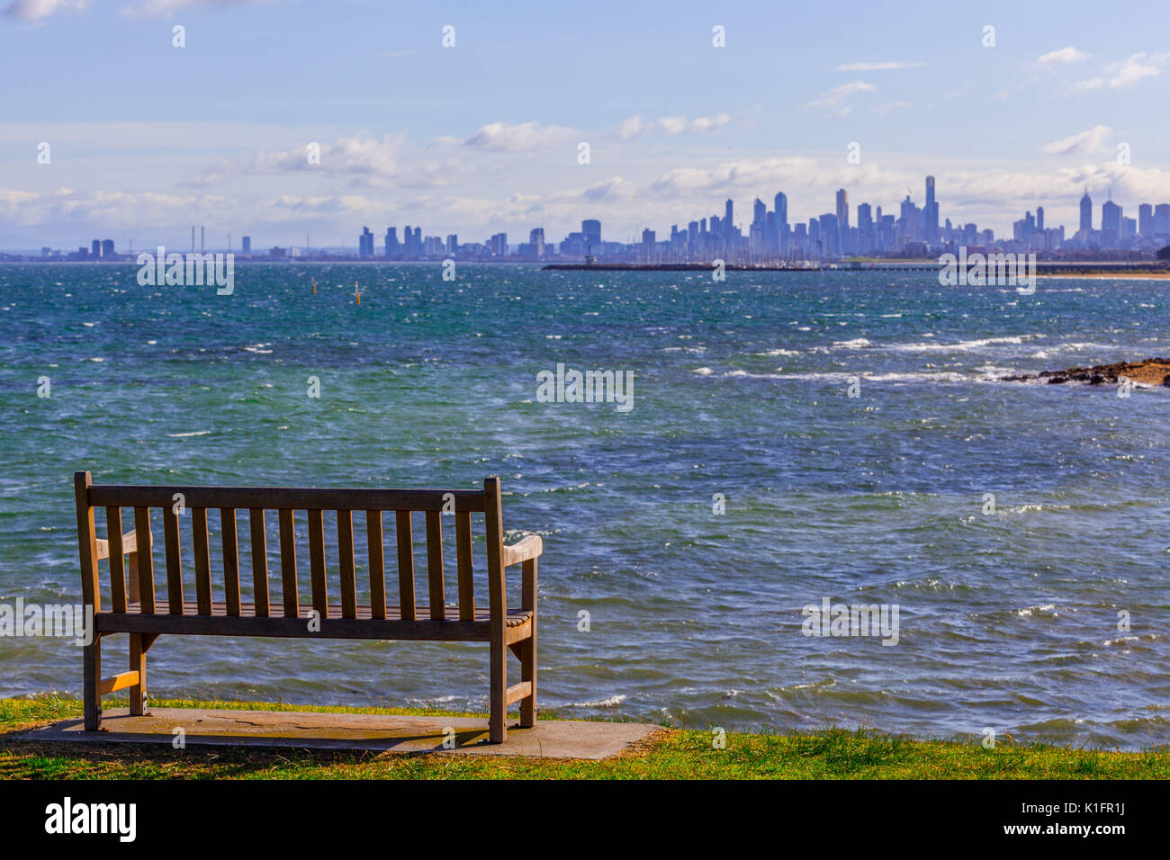Empty wooden bench on ocean shore overlooking the skyline of Melbourne ...