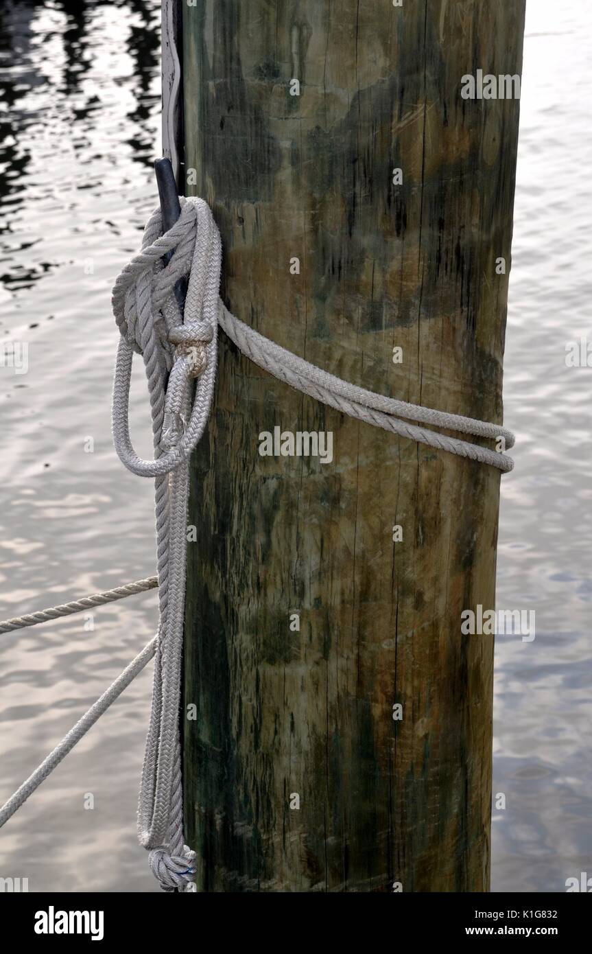 White nautical rope tied around a pylon with water in the background ...