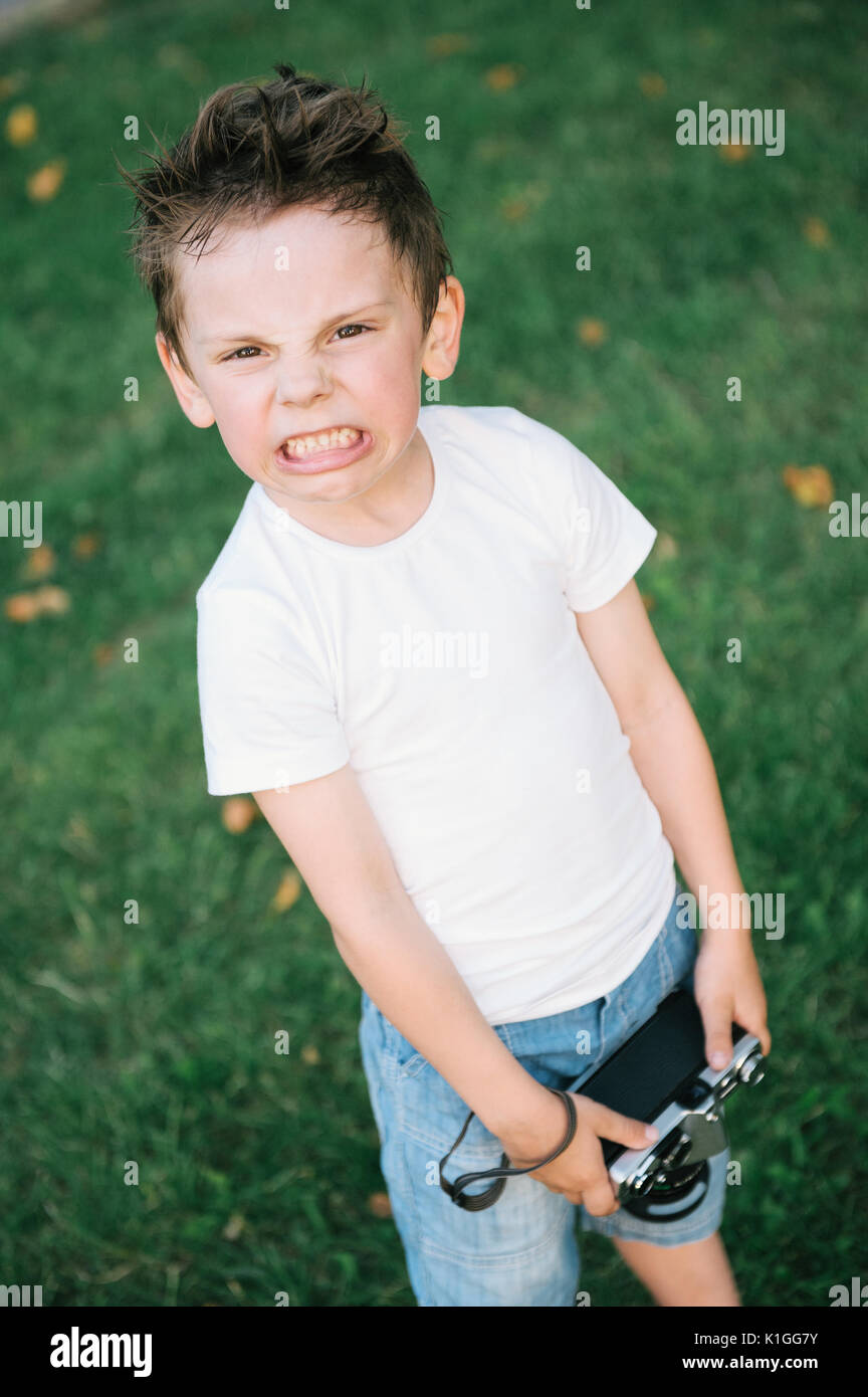 Angry little boy with a grimace on his face holding film camera on ...