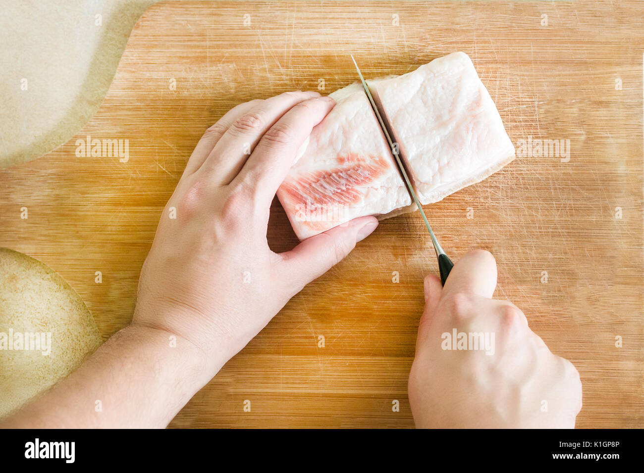 The top view of a man's hand cuts a piece of raw pork fat on wooden ...