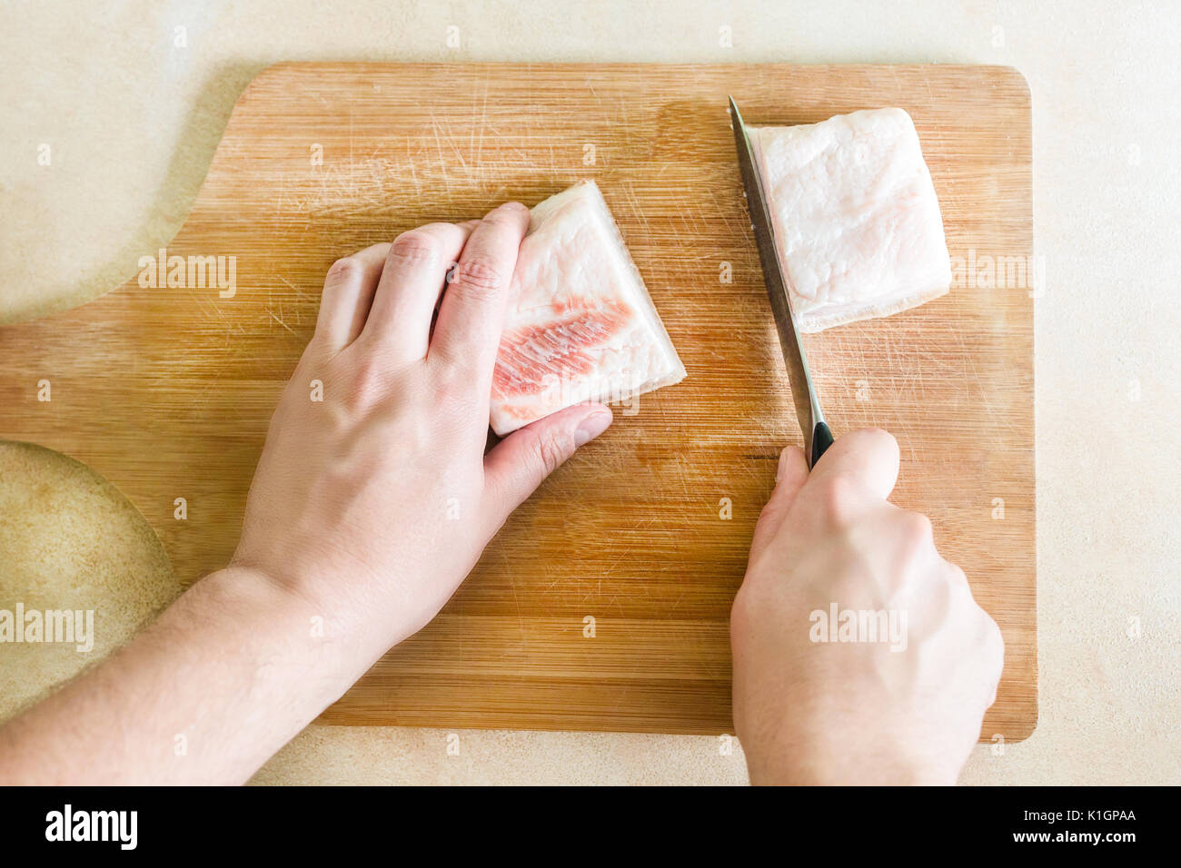 The top view of a man's hand cuts a piece of raw pork fat on wooden ...