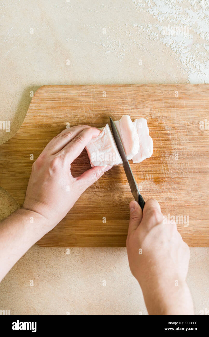 The top view of a man's hand cuts a piece of raw pork fat on slices ...