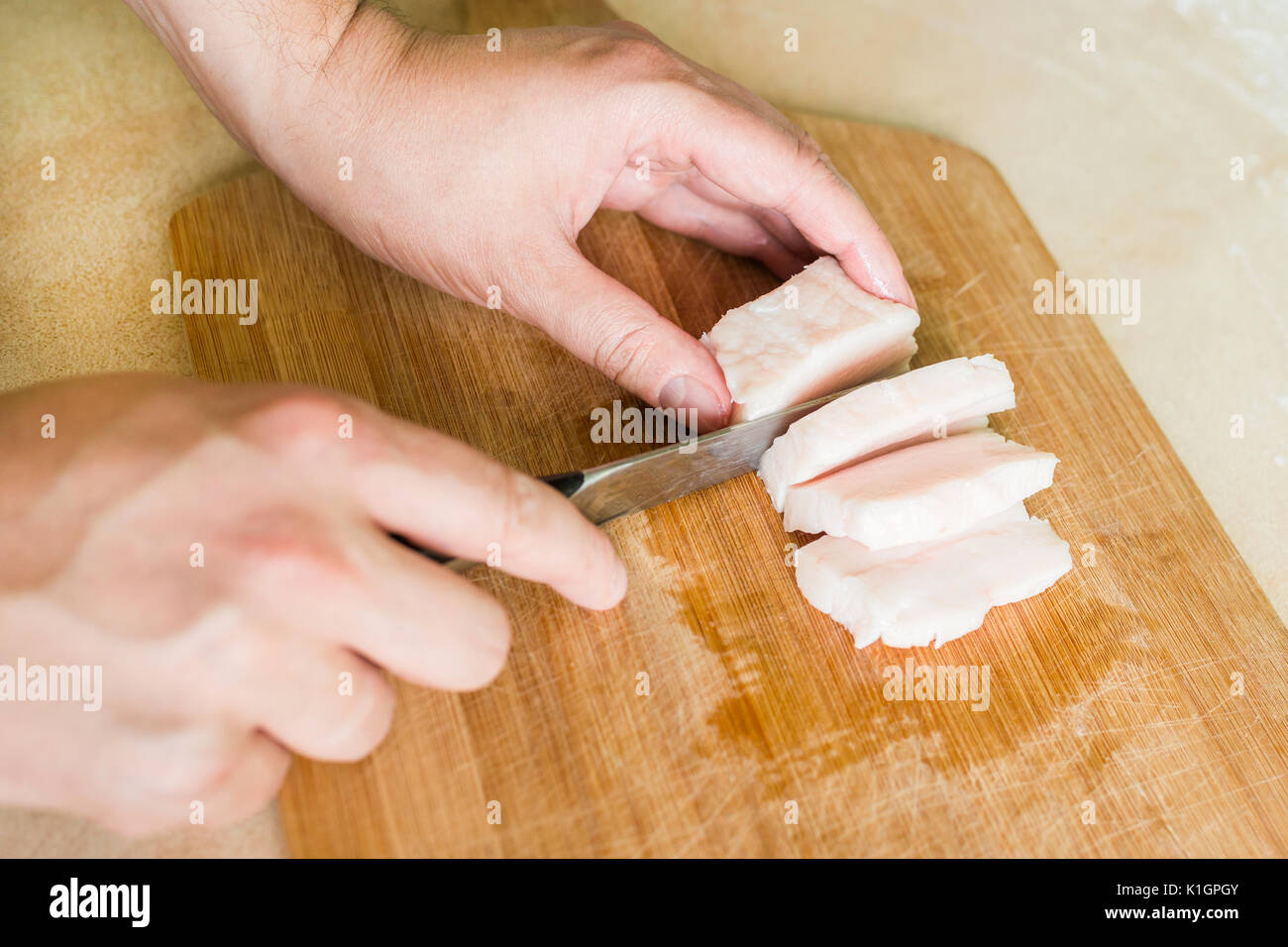 The side view of a man's hand cuts a piece of raw pork fat on slices ...