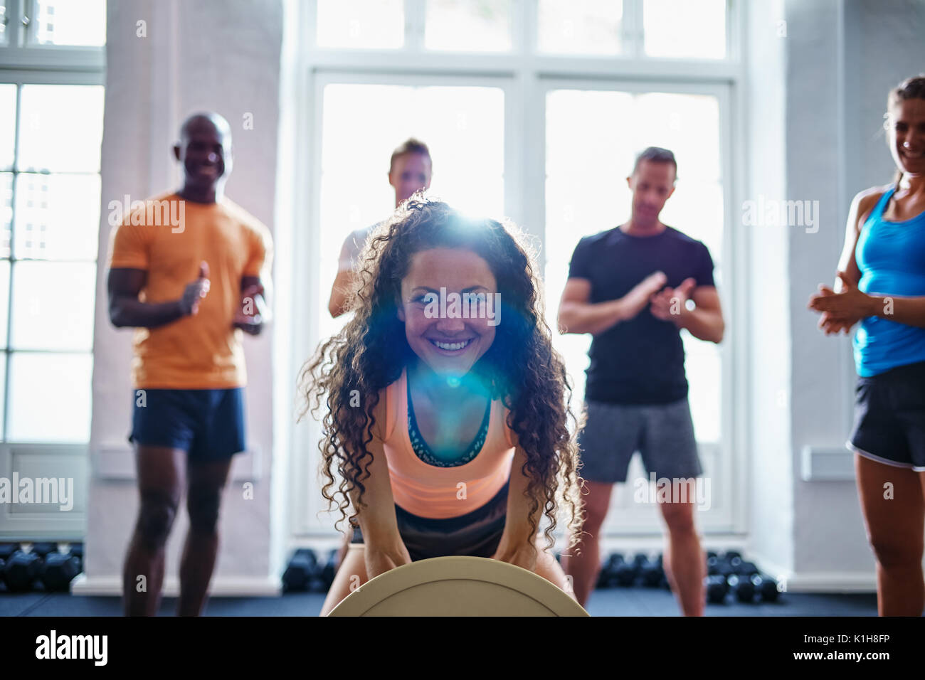 Smiling young woman weightlifting in a gym with a diverse group of ...