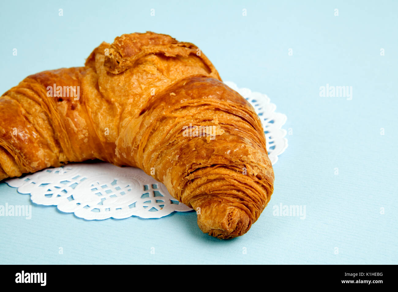 a french croissant on a doily lace paper. Pastel blue background ...